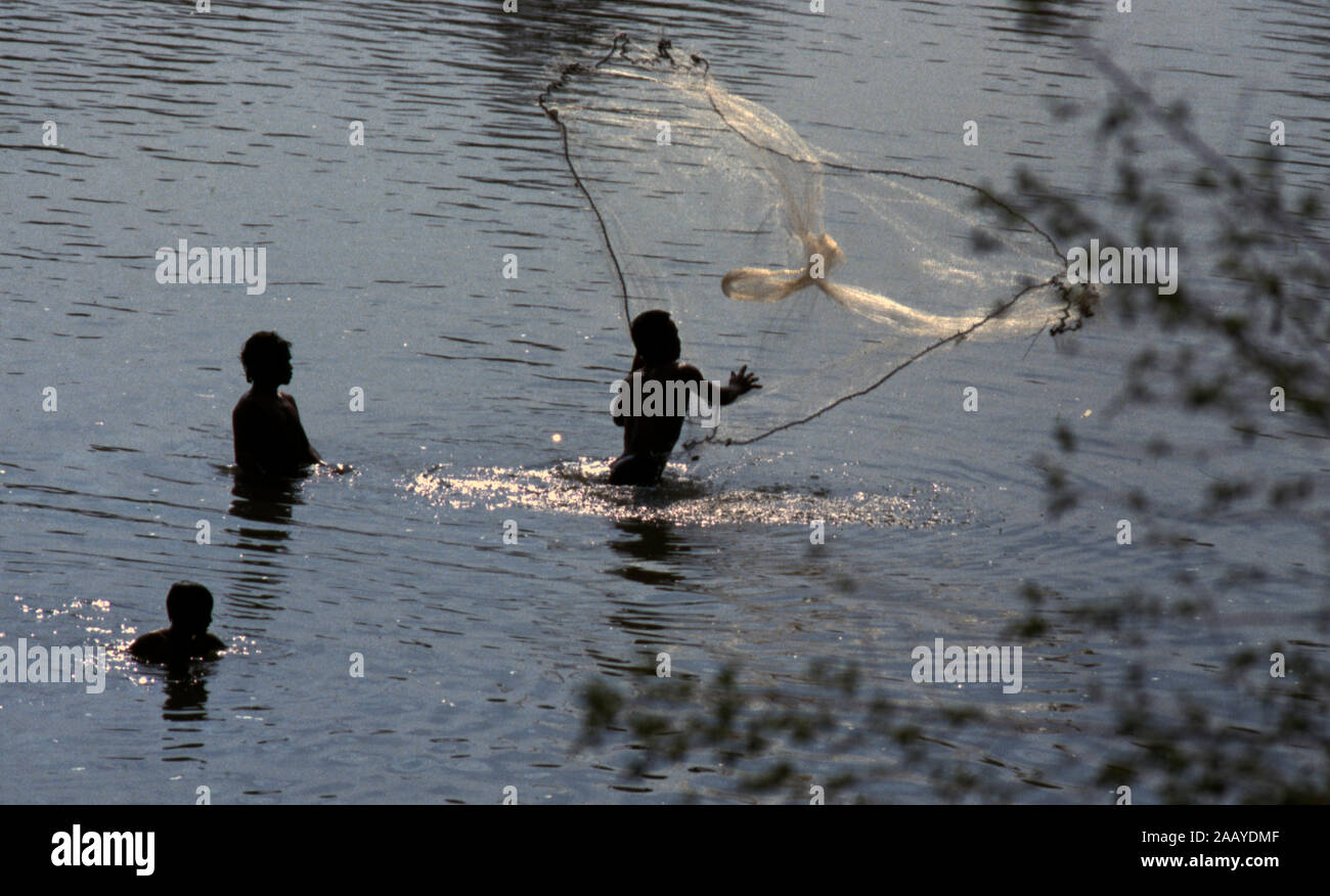 Indigenous Kachok tribe men cast a fishing net in a river near their ...