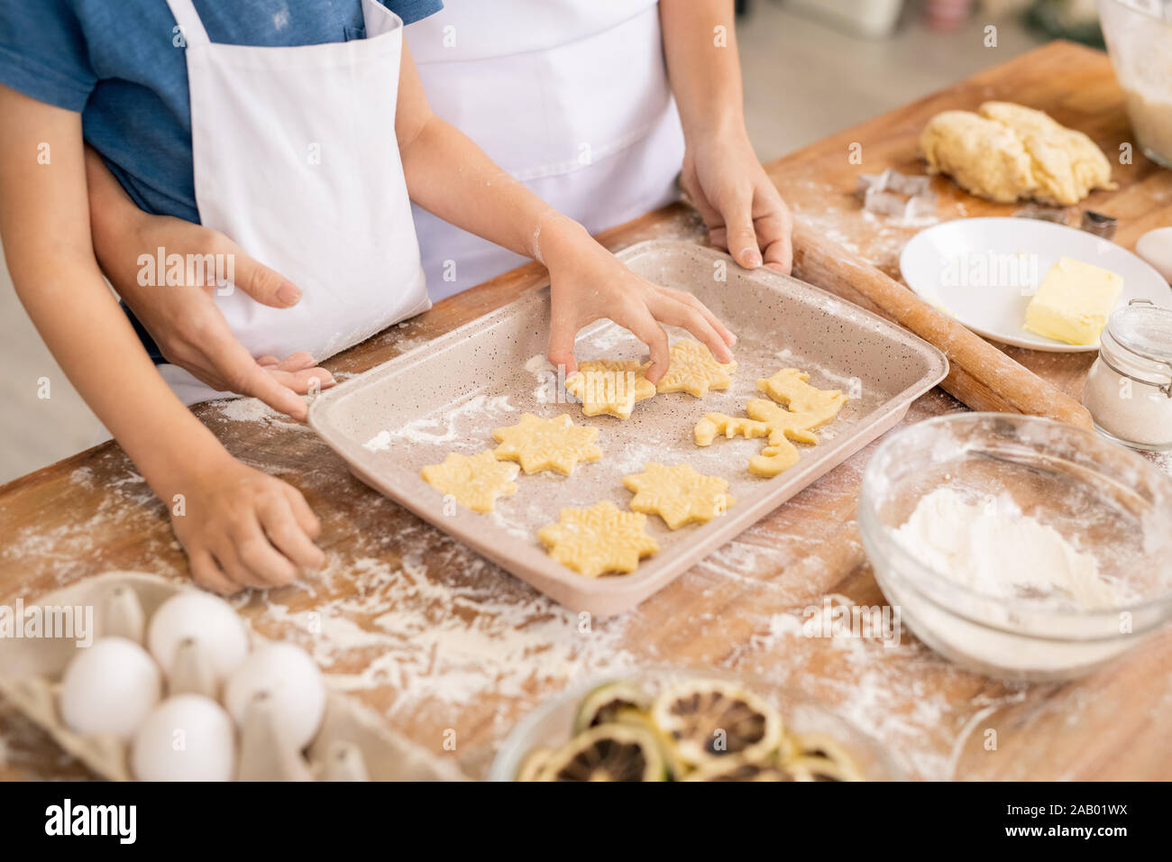 Hand of youngster putting raw biscuits on tray while helping mom with ...