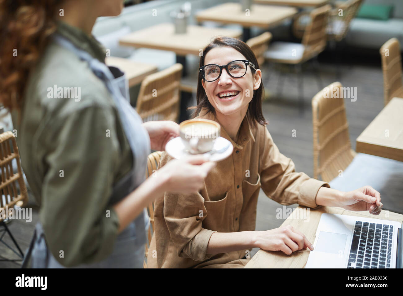 High angle portrait of young woman smiling at waitress while working at ...