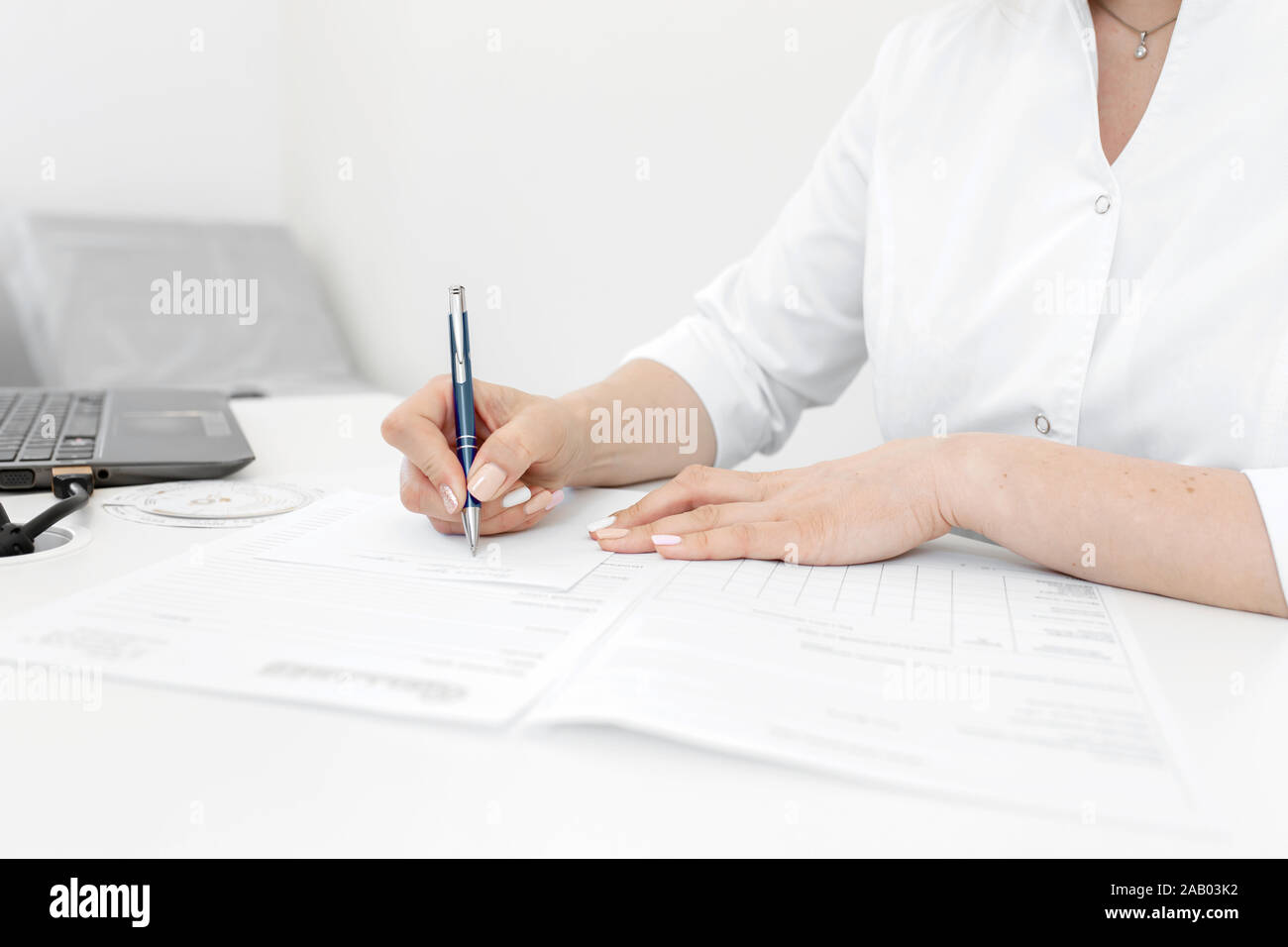 Portrait of a blonde doctor woman in a white coat sitting at a table in ...