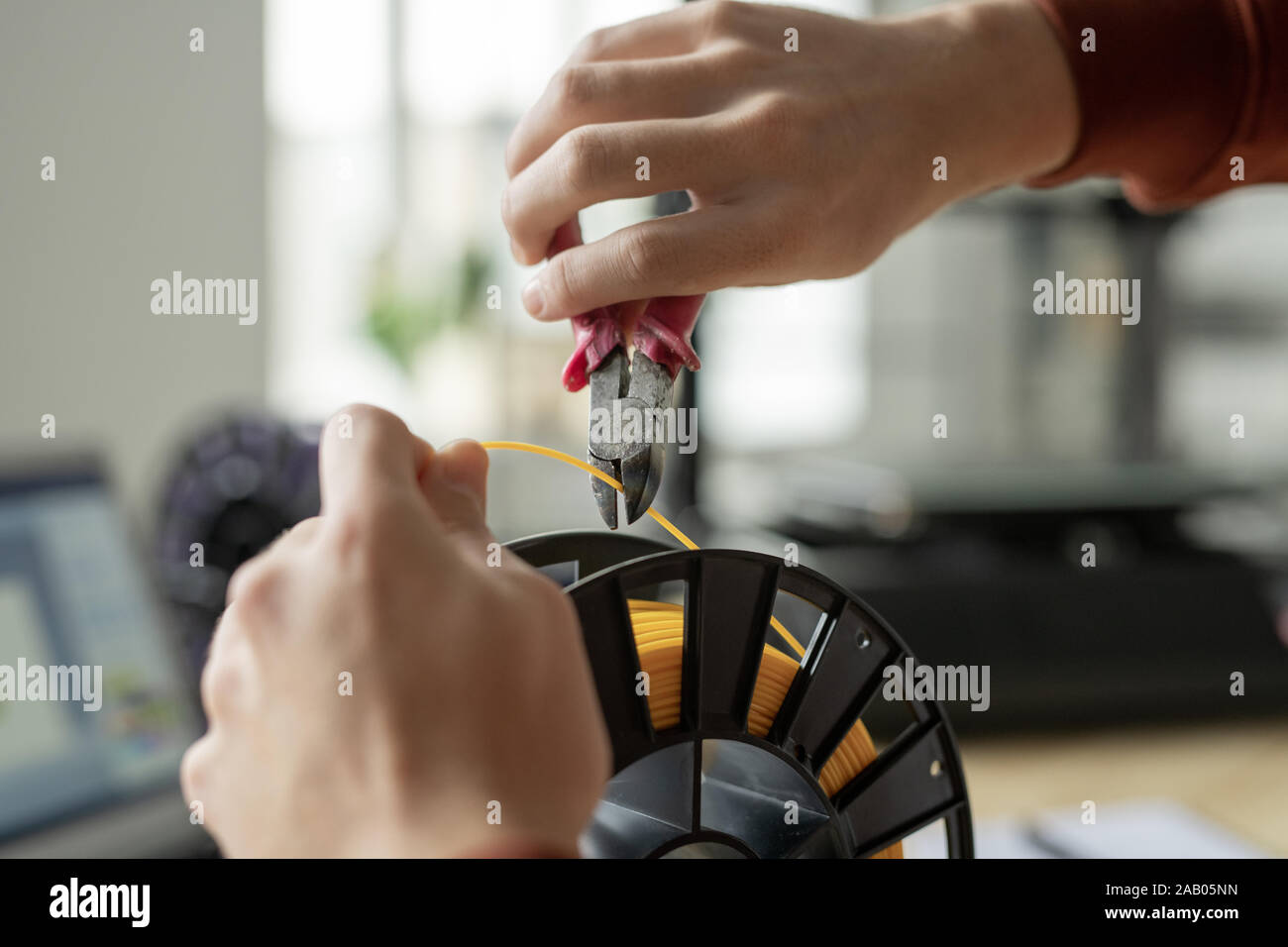 Hands of guy with nippers cutting piece of yellow filament on spool to ...