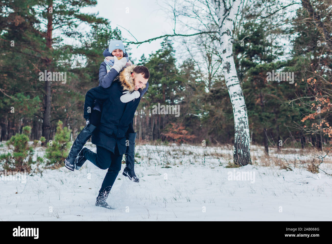 Man giving his girlfriend piggyback in winter forest. Couple in love ...
