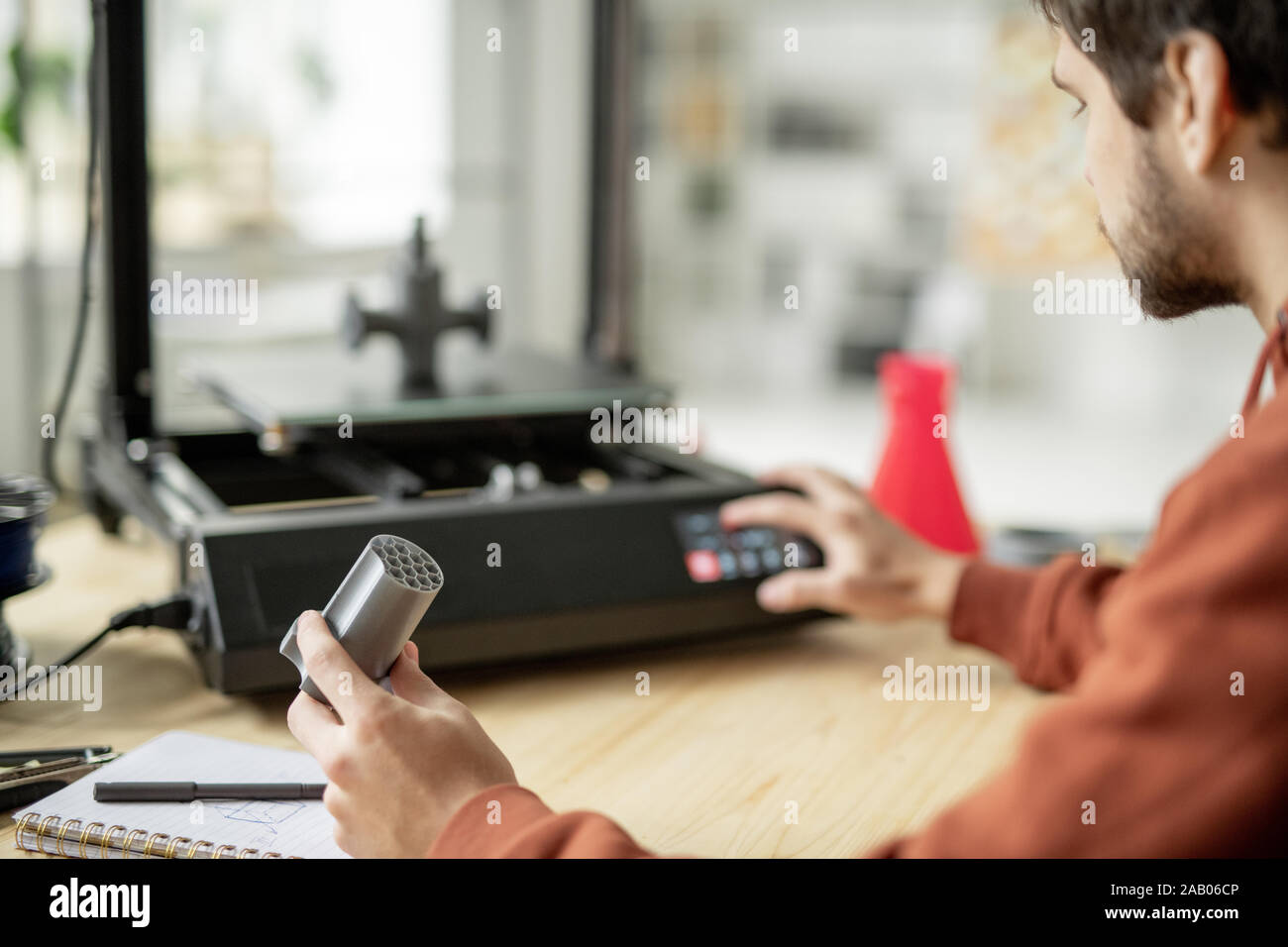 Young engineer holding detail of 3d printer while checking if the ...