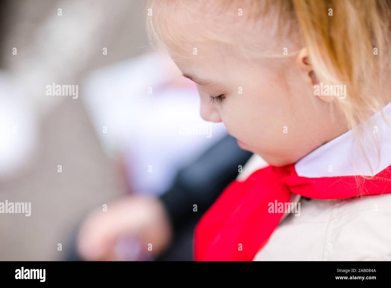 Smiling scholar girl sitting with other children in classroom and writing on textbook. Happy ...