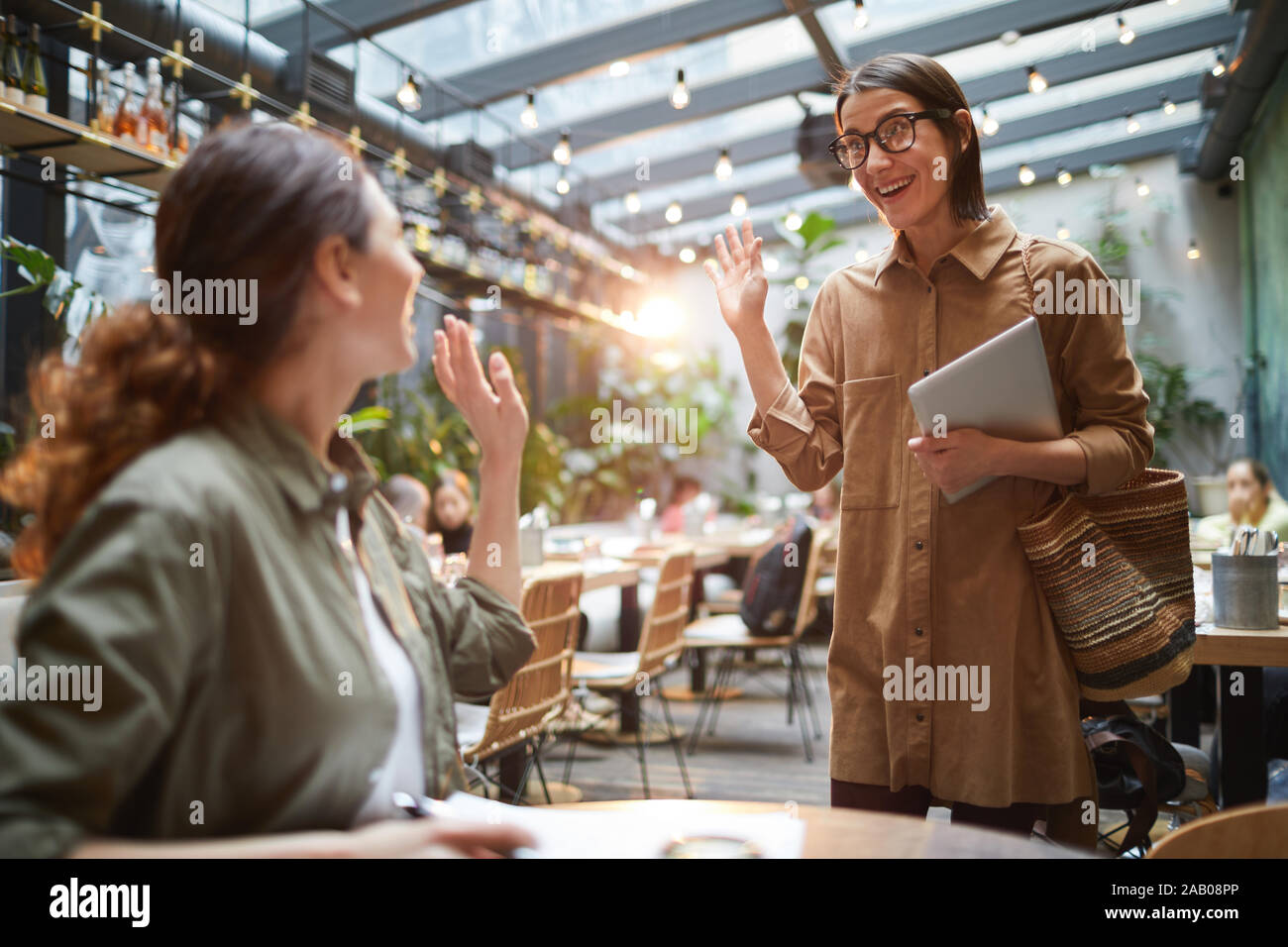 Portrait of two young women waving at each other during meeting in cafe ...