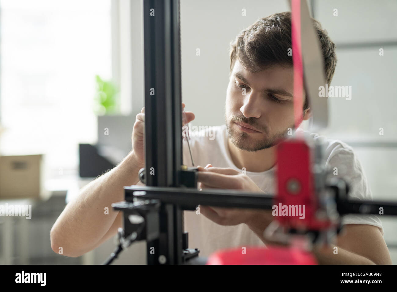 Young businessman standing in front of 3d printer while fixing some ...