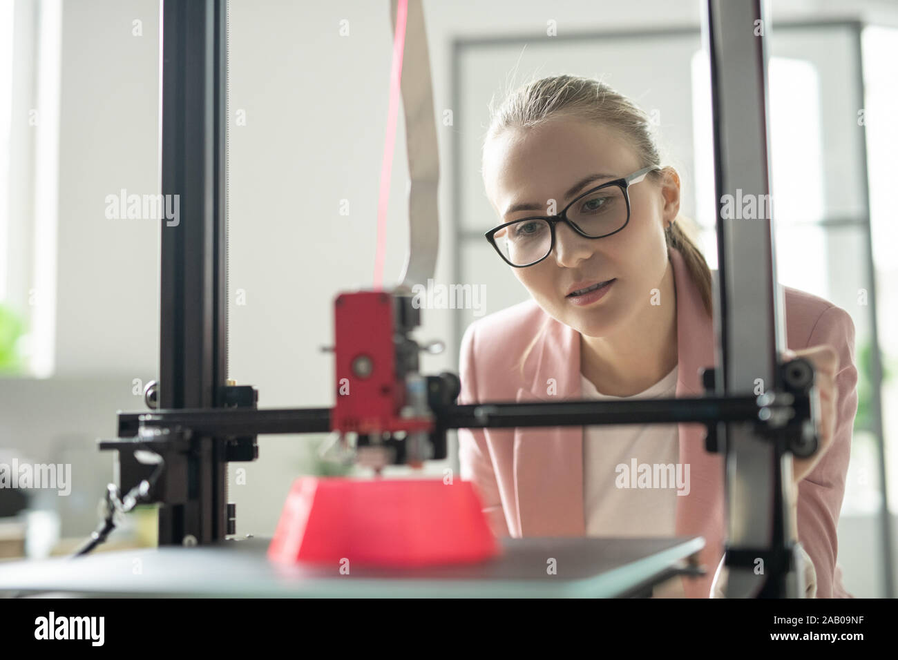 Young businesswoman standing in front of 3d printer in process of ...