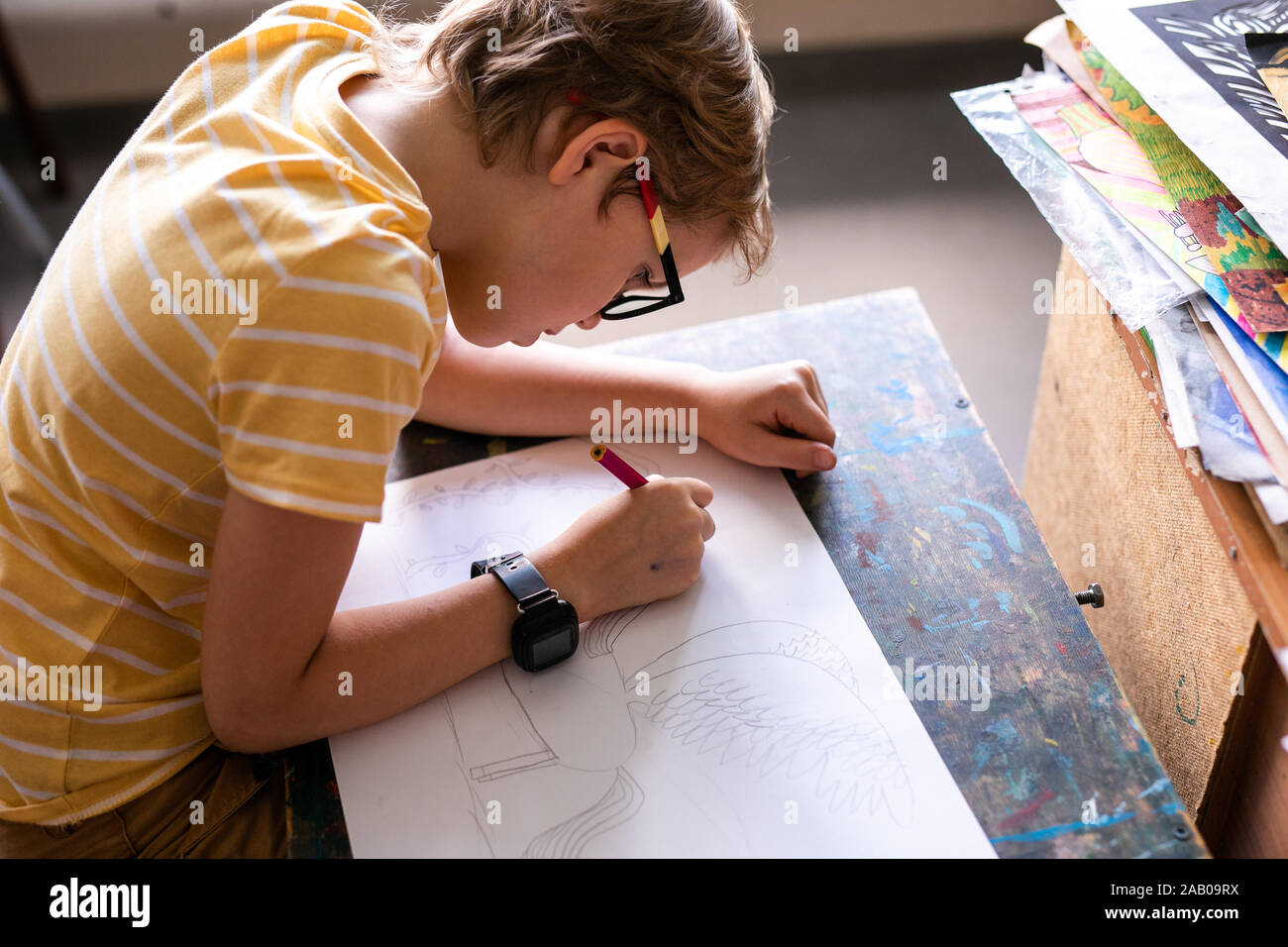 Portrait of cute boy with sketch pen and paper at desk in classroom ...