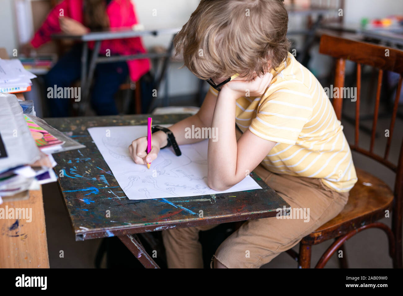 Portrait of cute boy with sketch pen and paper at desk in classroom ...