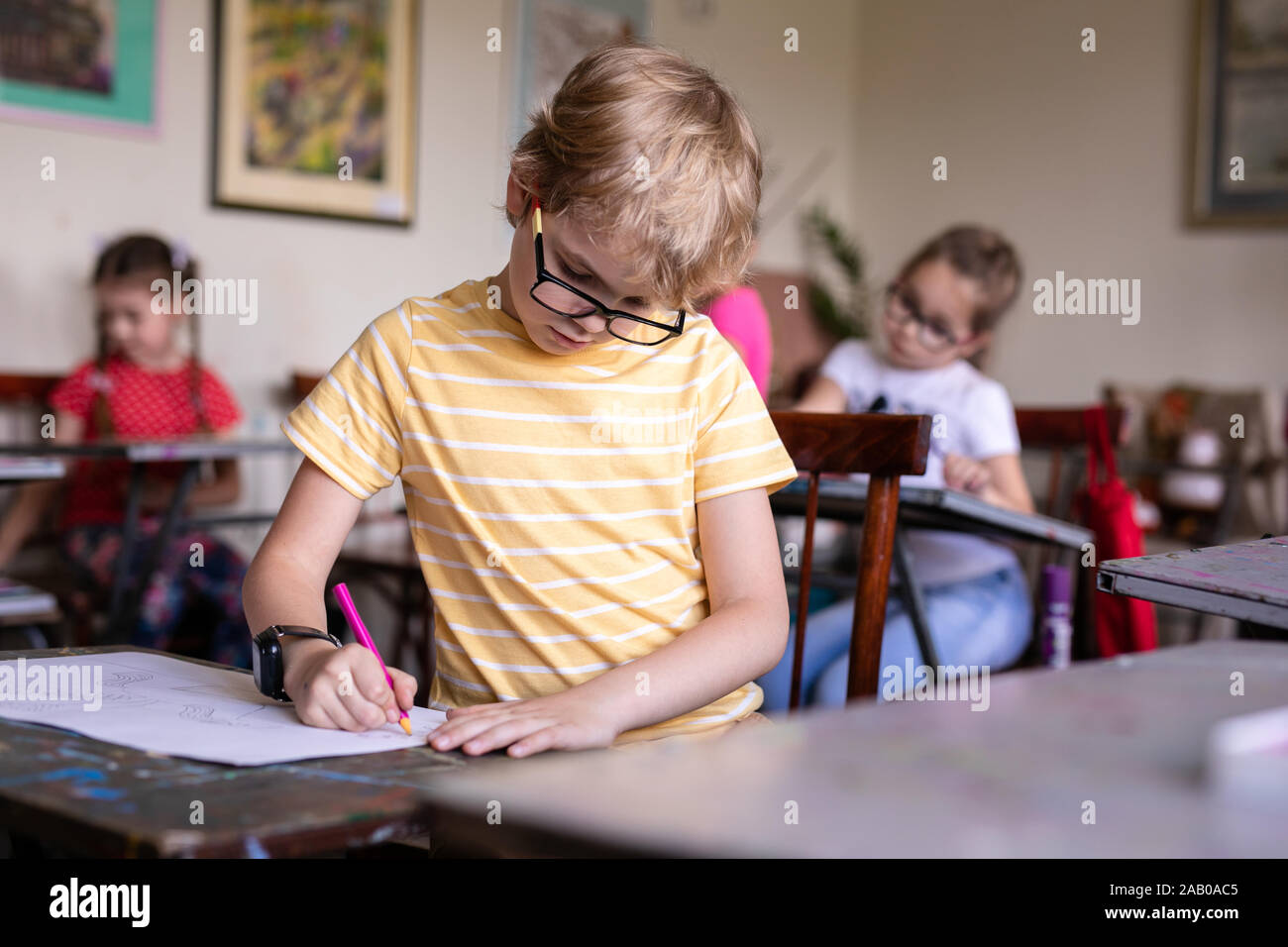 Portrait of cute boy with sketch pen and paper at desk in classroom ...