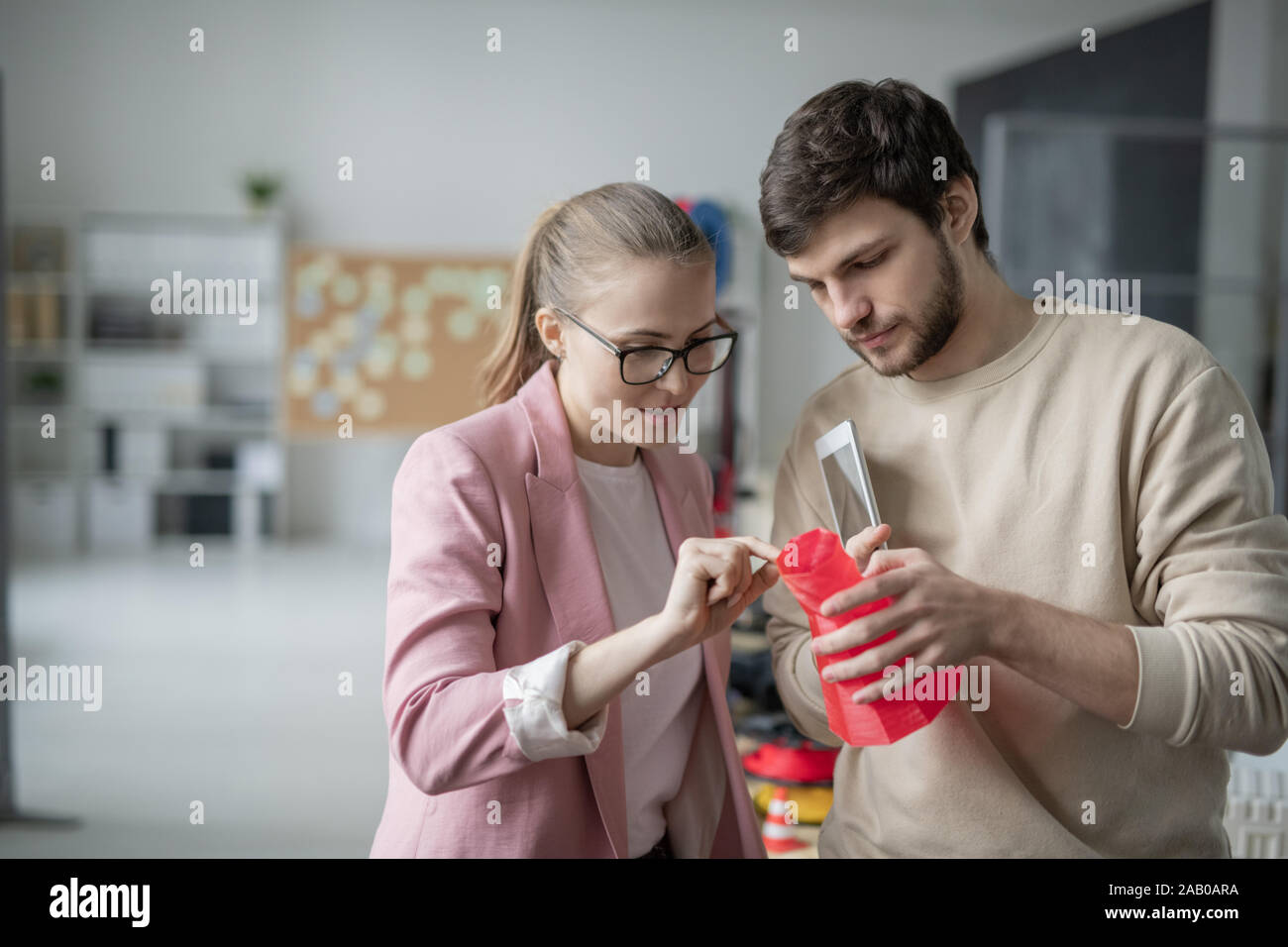 Young colleagues discussing red geometric object just printed in 3d ...