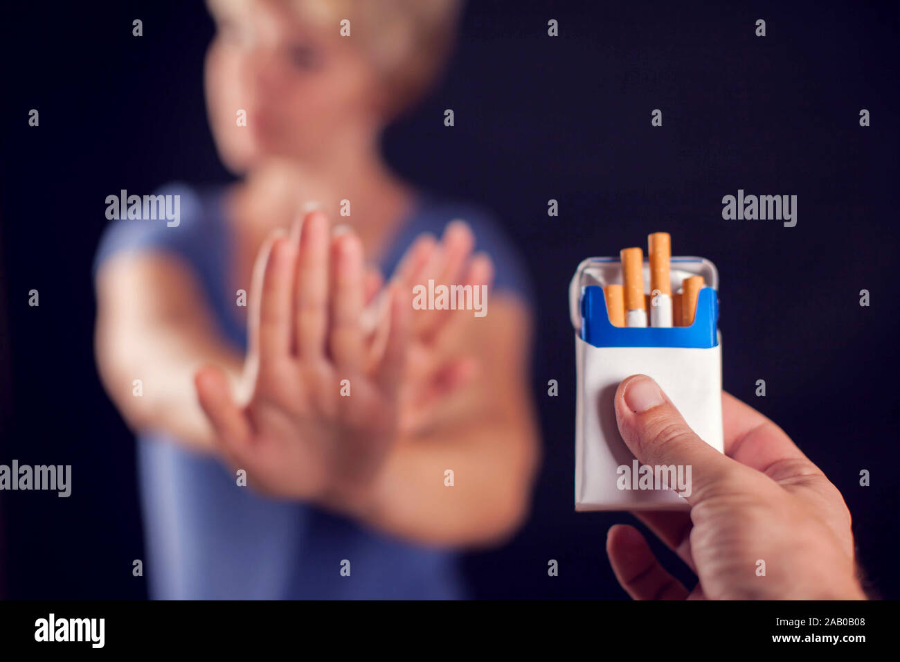 Woman in blue t-shirt refusing cigarettes on black background. Stop ...