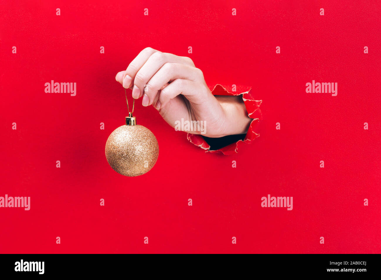 Female hand holding golden Christmas tree bauble through a hole in red ...