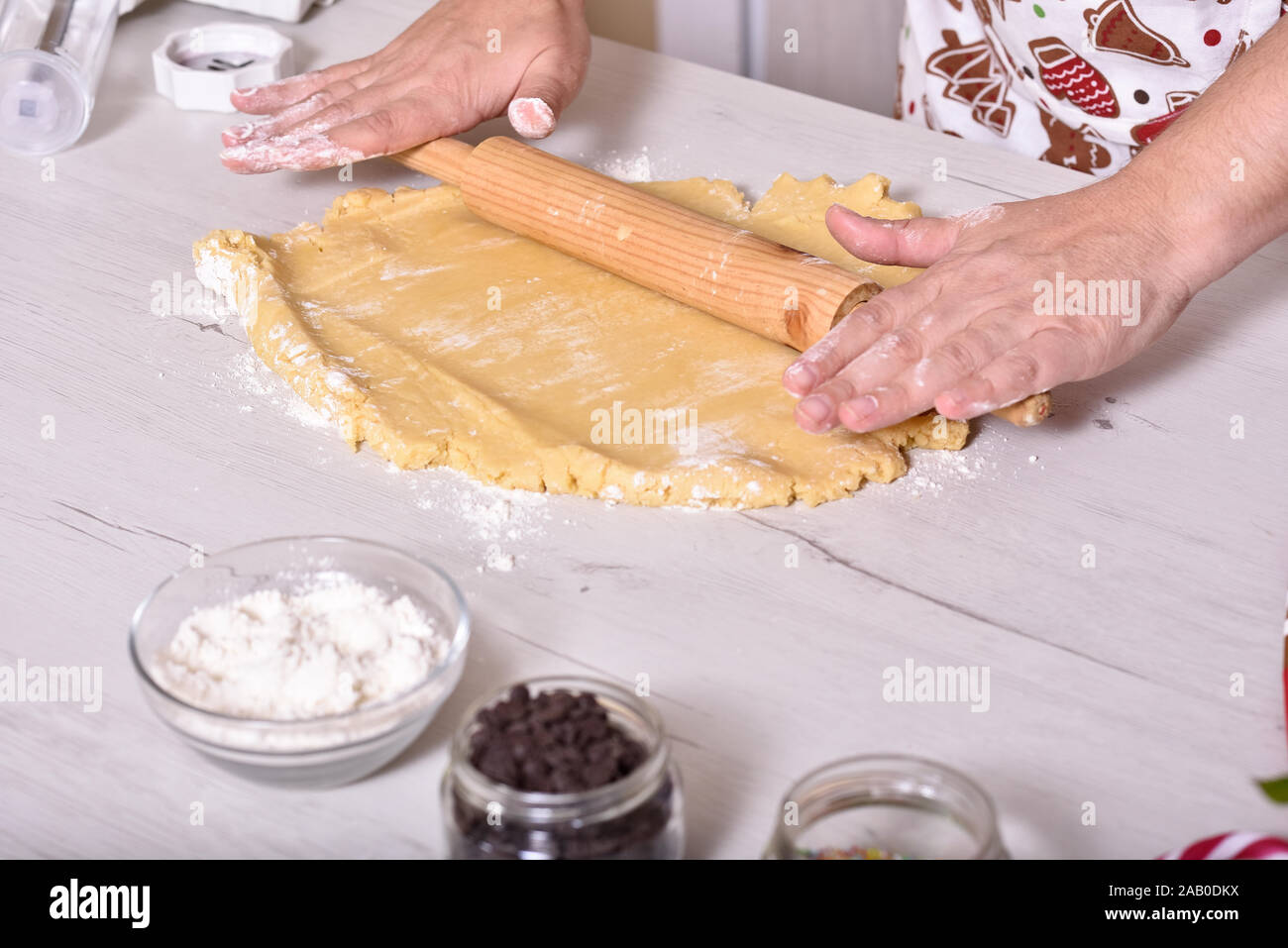 Close-up of female hands rolling dough with pin on wooden table ...