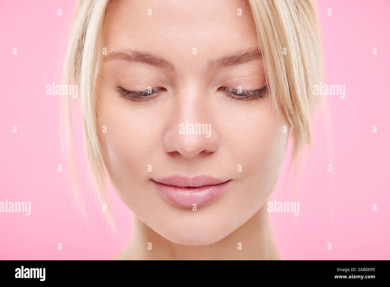 Pretty young blond natural woman looking down over pink background ...