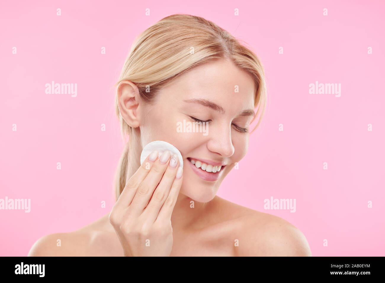 Pretty young smiling female with cotton pad enjoying procedure of ...
