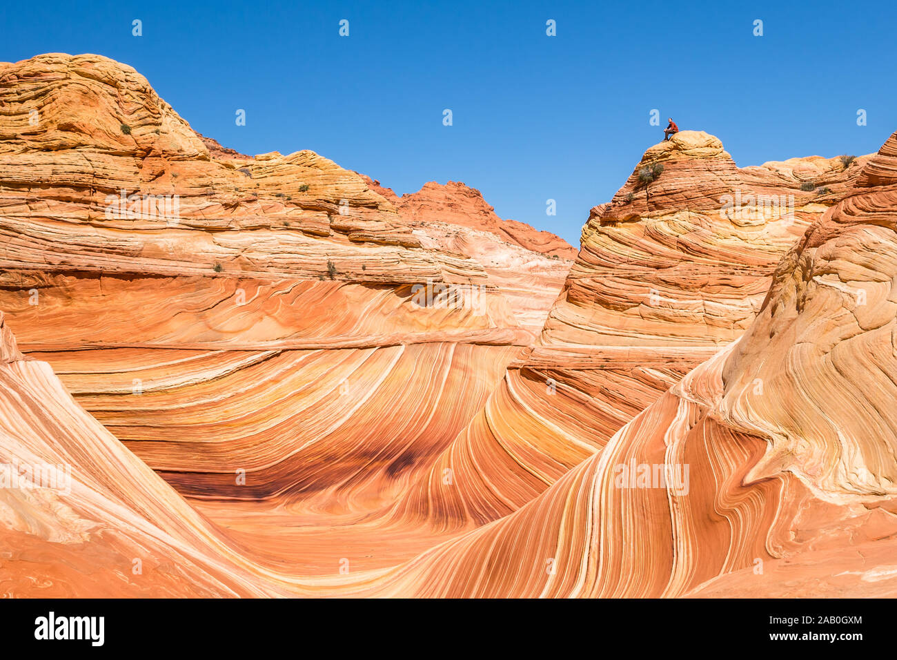 Hiker or rock climber sitting atop the summit of a sandstone dome above ...