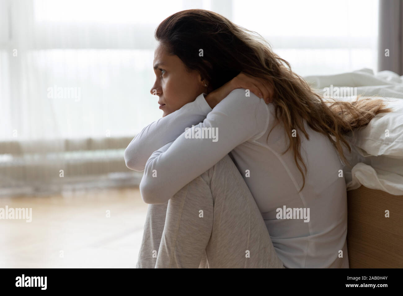 Sad woman sitting on floor leaned on bed feels lonely Stock Photo - Alamy