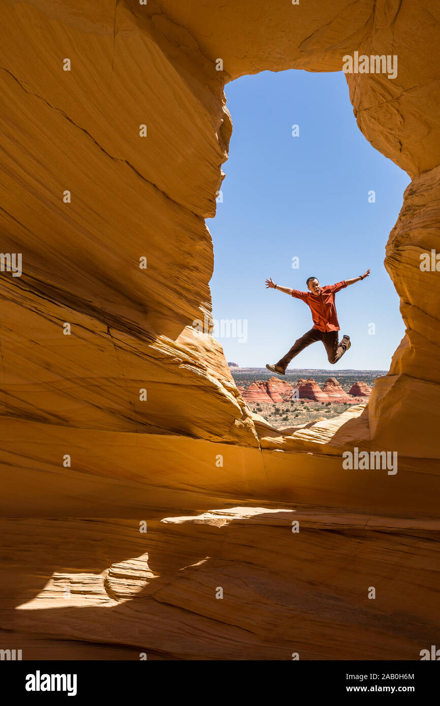 Man in red and brown, hiker jumping for joy in the window of an arch in ...