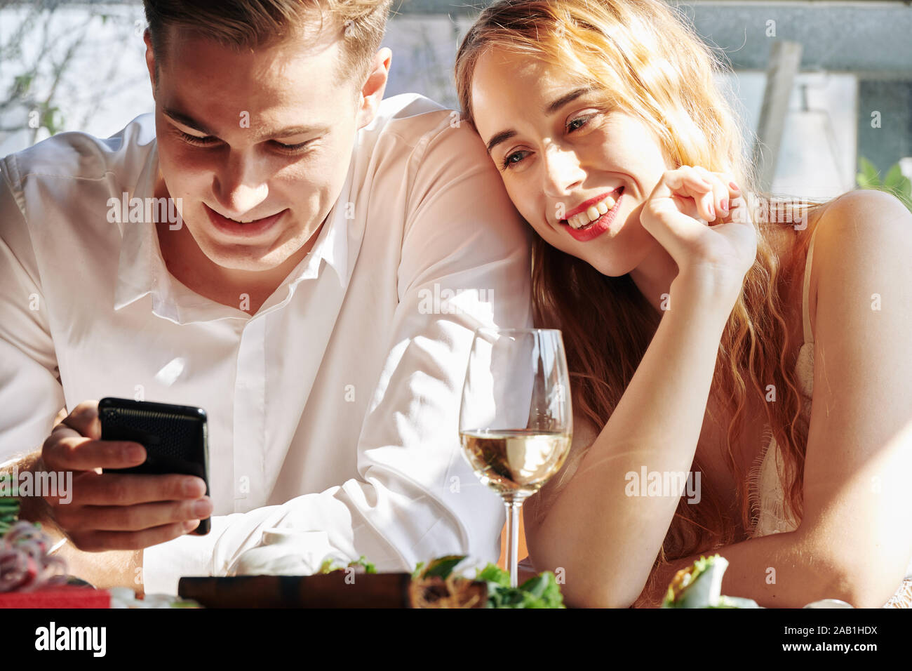 Cheerful young couple checking social media on smartphone during dinner ...