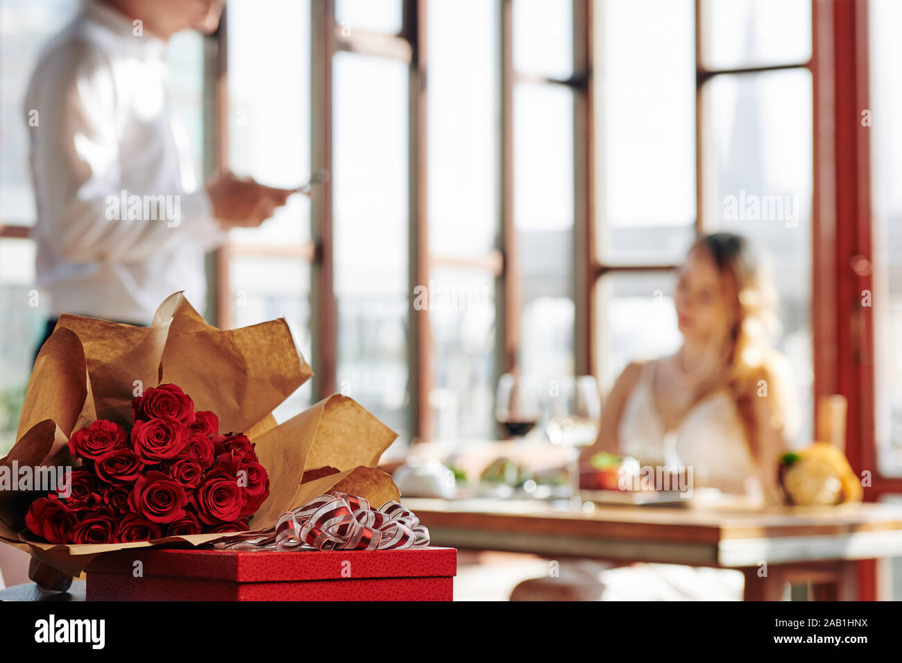 Bouquet of fresh red roses and a gift, waiter talking to female ...