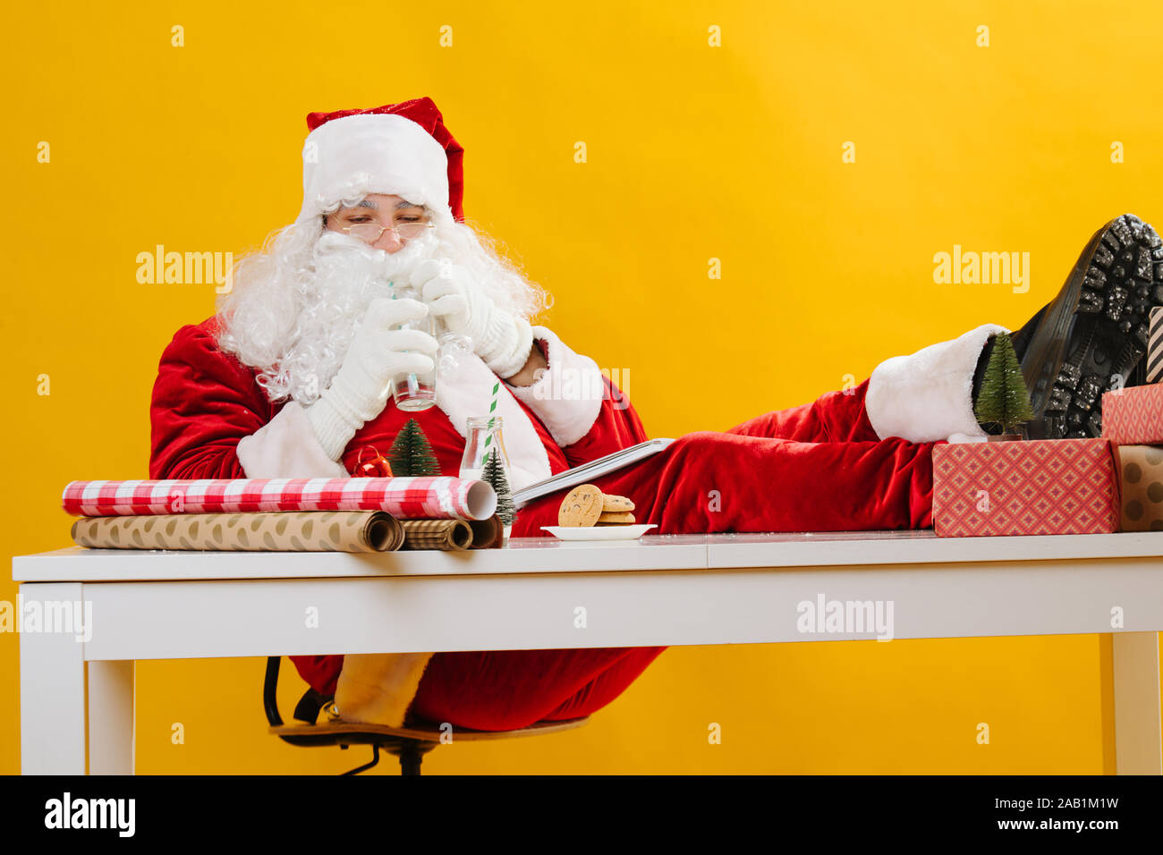 Santa Claus working behind a desk in comfort, drinking milk with legs ...
