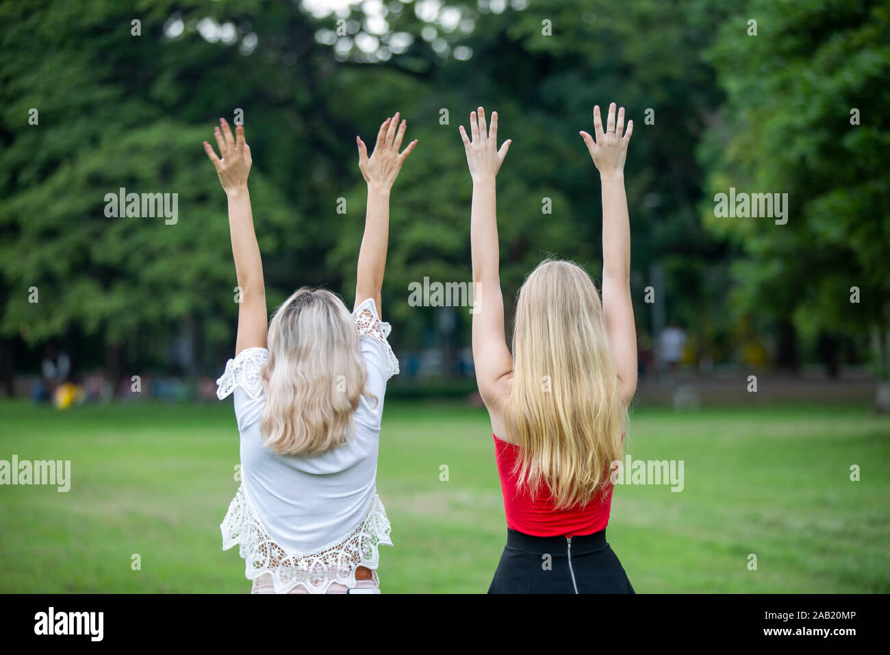 two young women hand raise up against tree Stock Photo - Alamy