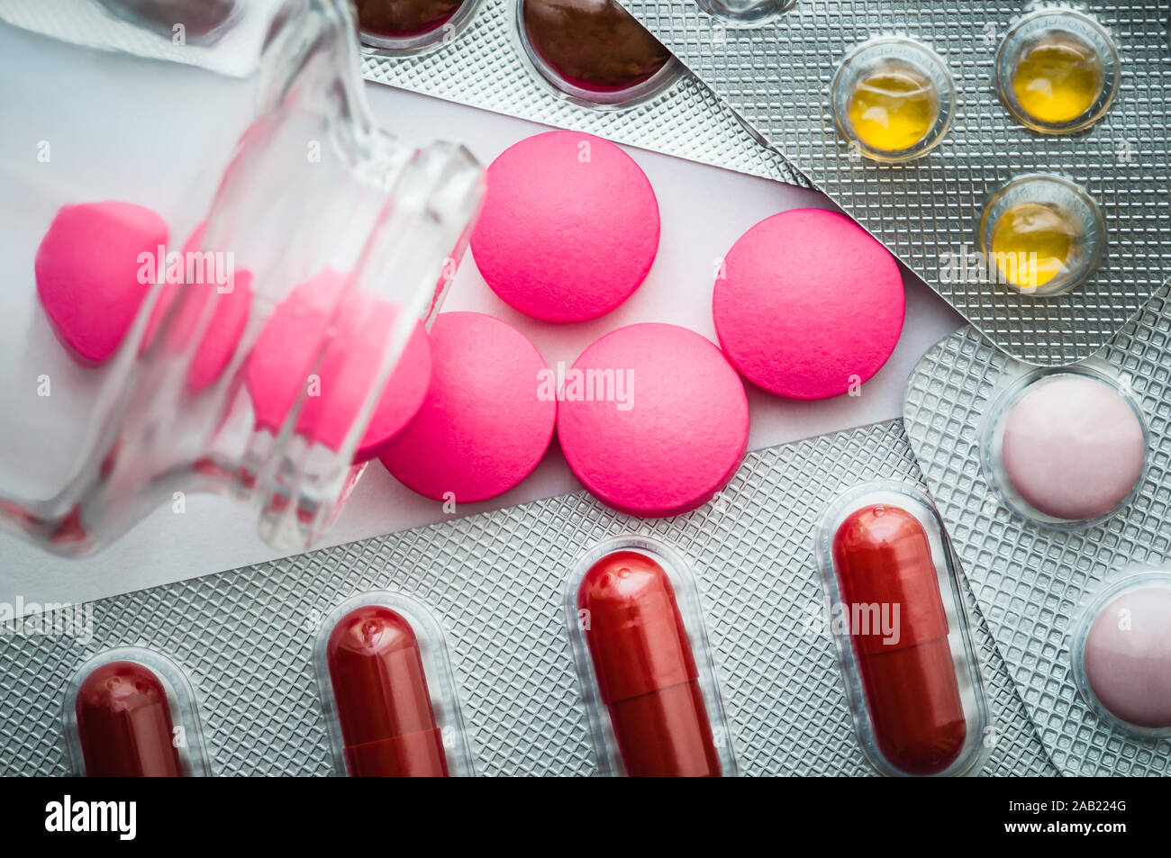Pink pills are poured from a glass jar and blisters with colored ...