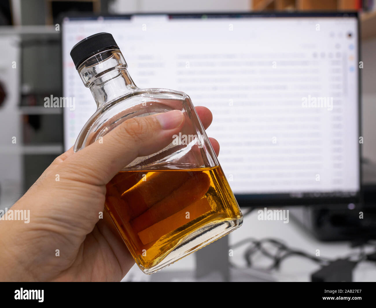 Hand holds a bottle of whiskey inf ront of a computer screen. Drinking ...