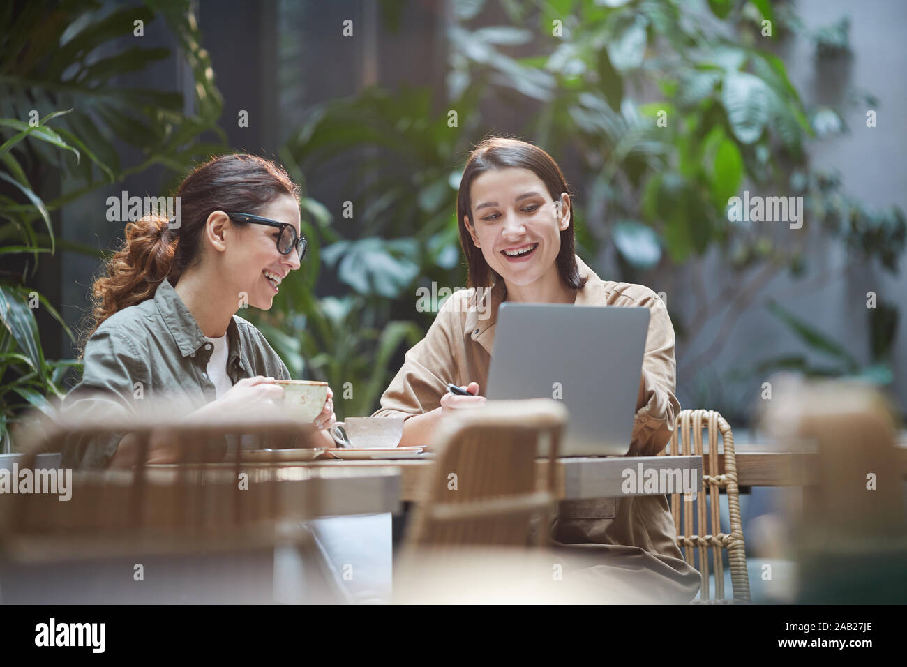 Portrait of two young women laughing happily while using laptop on ...
