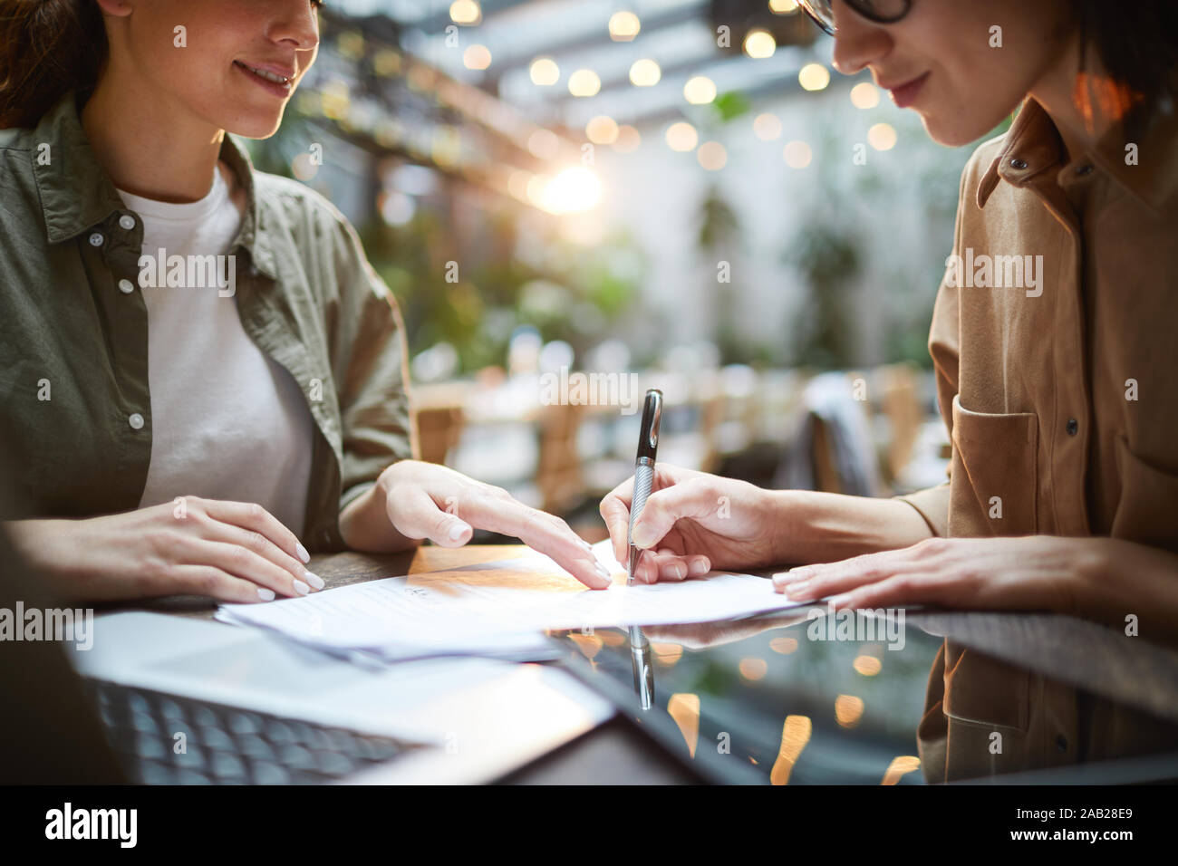 Close up of two young women signing contract during business meeting in ...