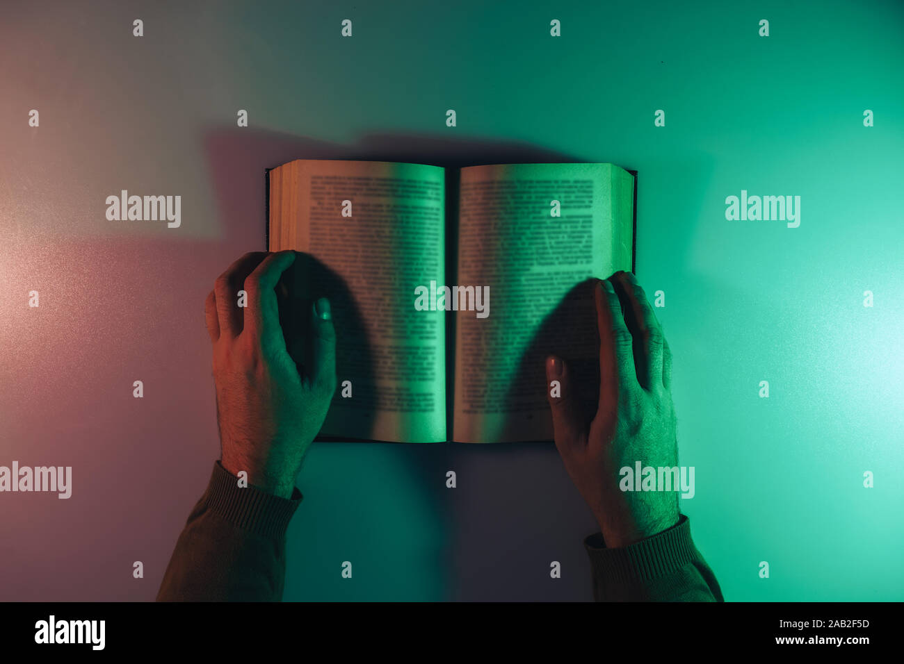 Beautiful man reading book in the color light on a table and night ...