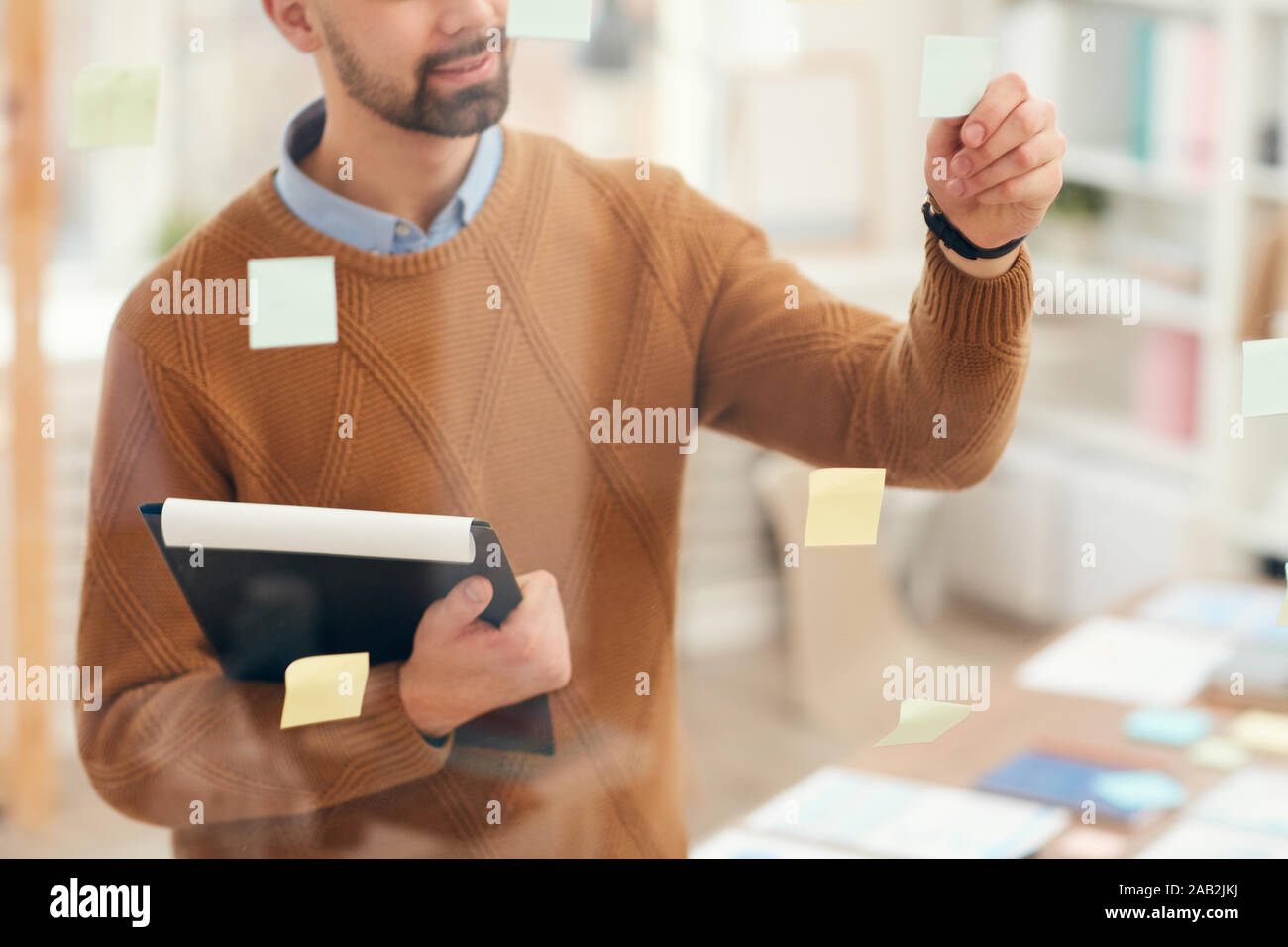 Mid-section portrait of bearded man placing sticker notes on glass wall ...