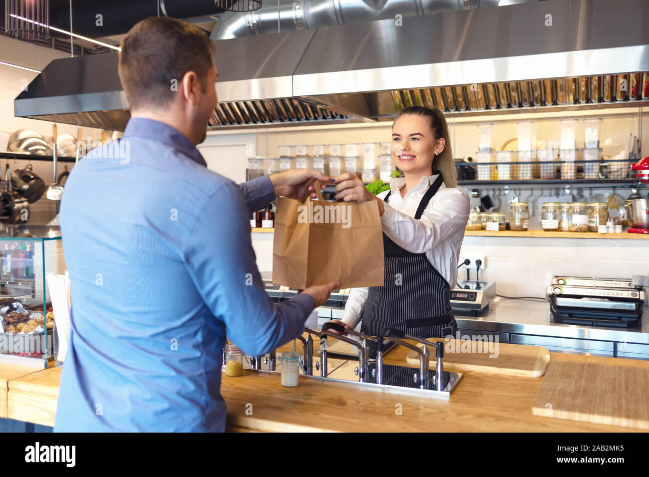 Happy waitress wearing apron serving customer at counter in small ...