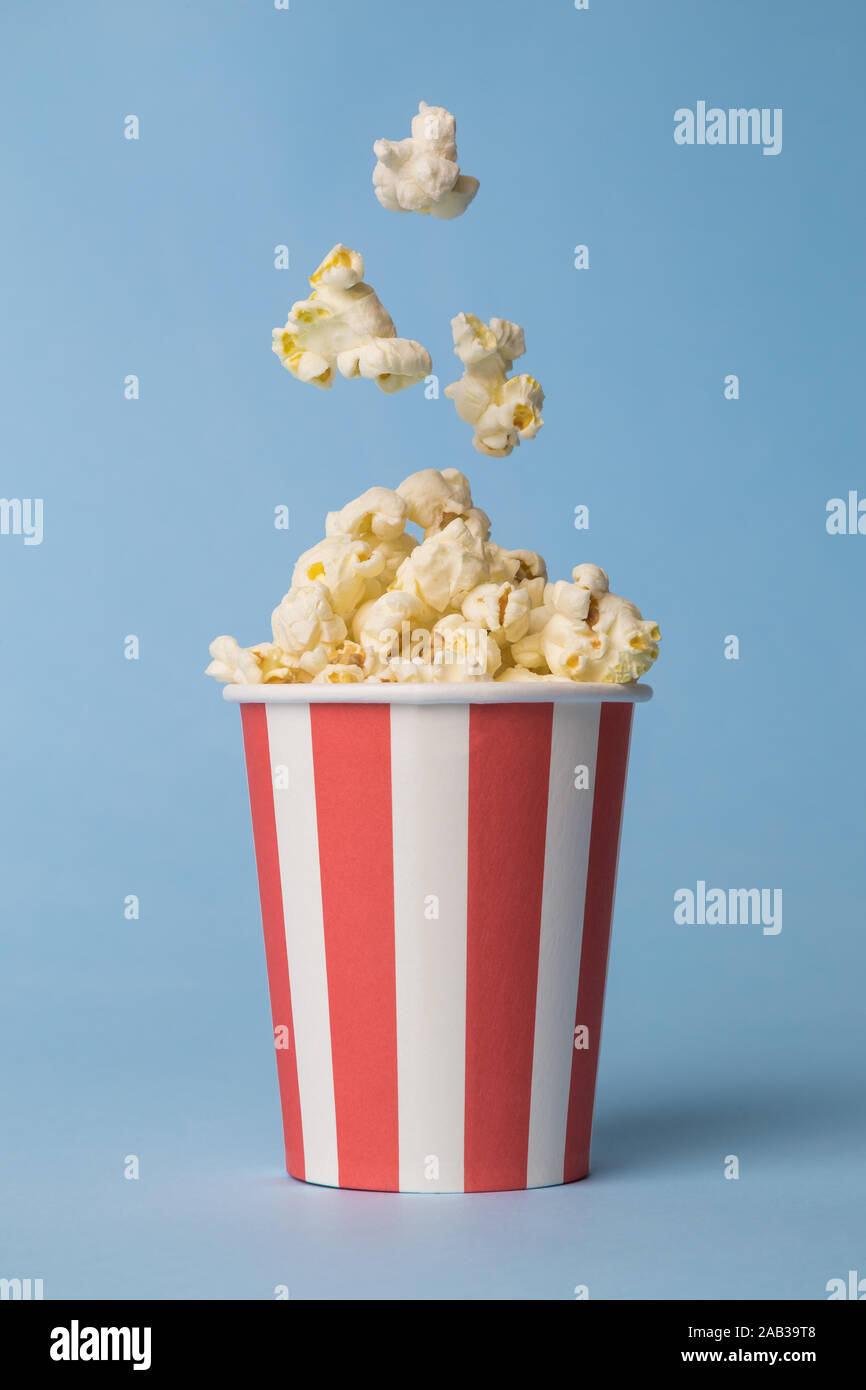 Popcorn falling into paper cup against pastel blue background minimal ...