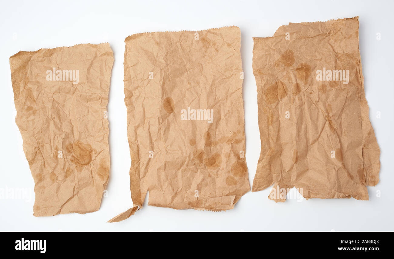 three torn crumpled pieces of brown paper with grease stains on a white ...