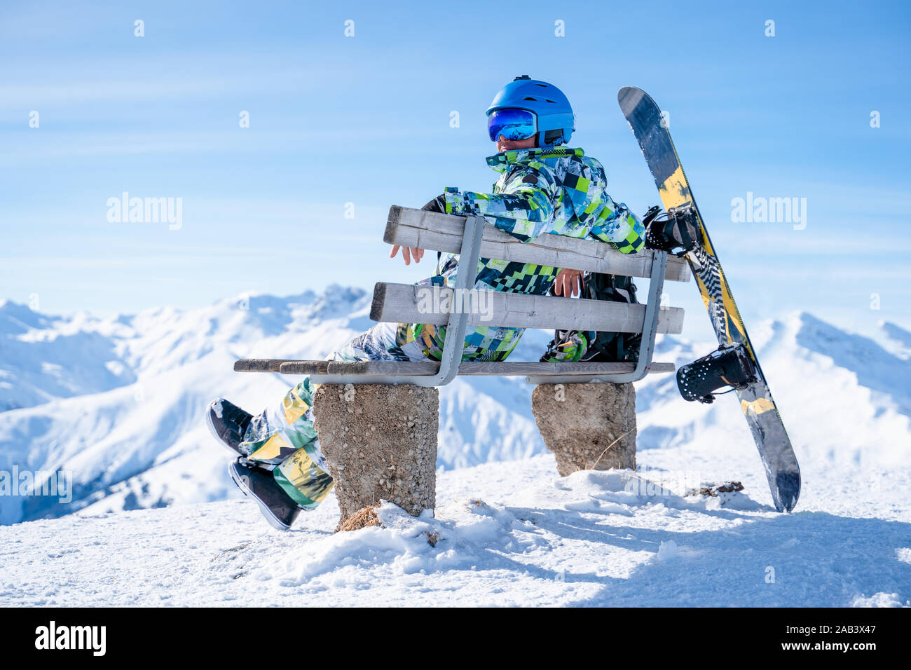 Photo from back of sportsman sitting on bench next to snowboard in ski ...