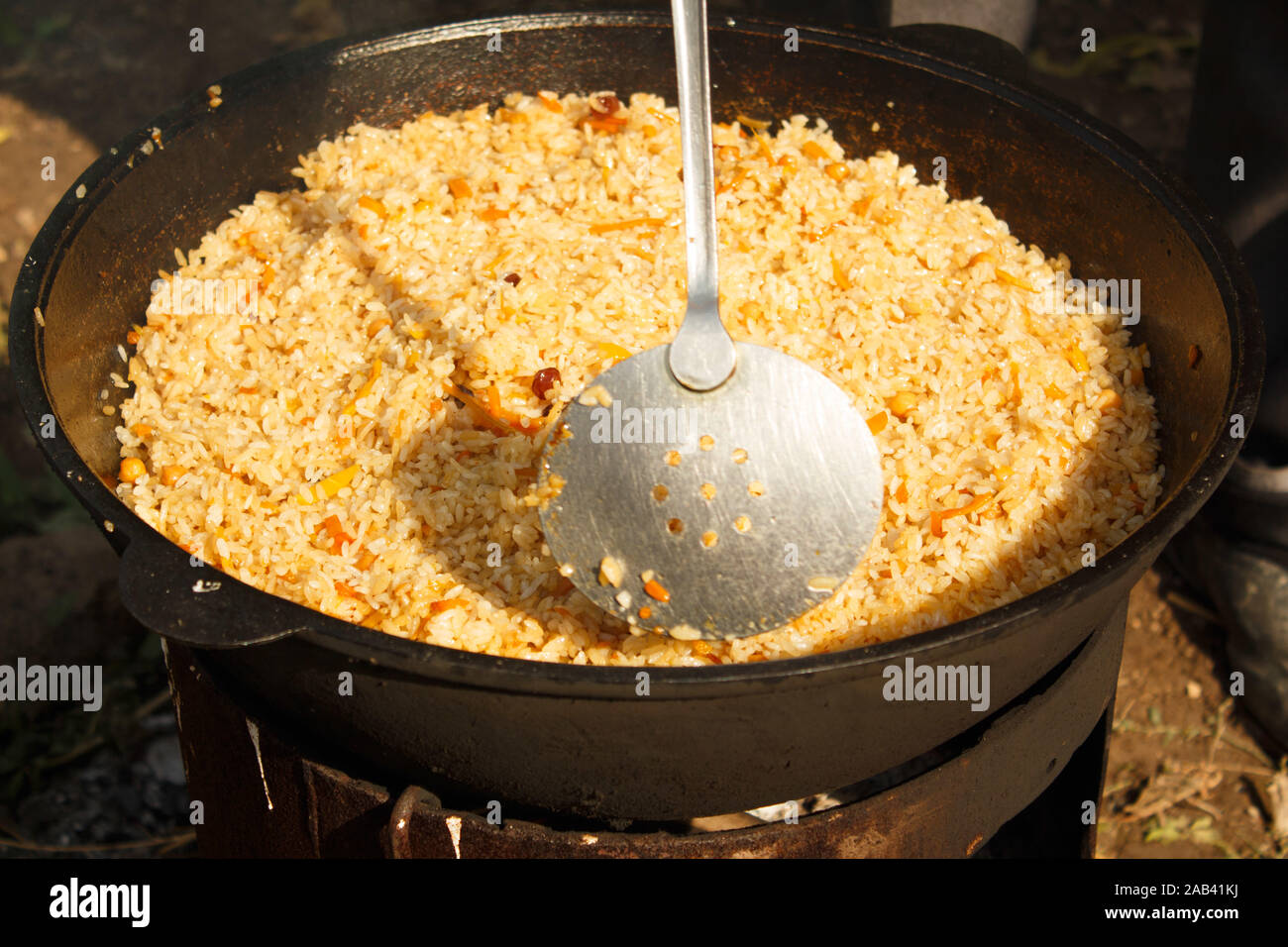 Cooking Uzbek pilav of rice and, carrot and meat in metal pan outside ...