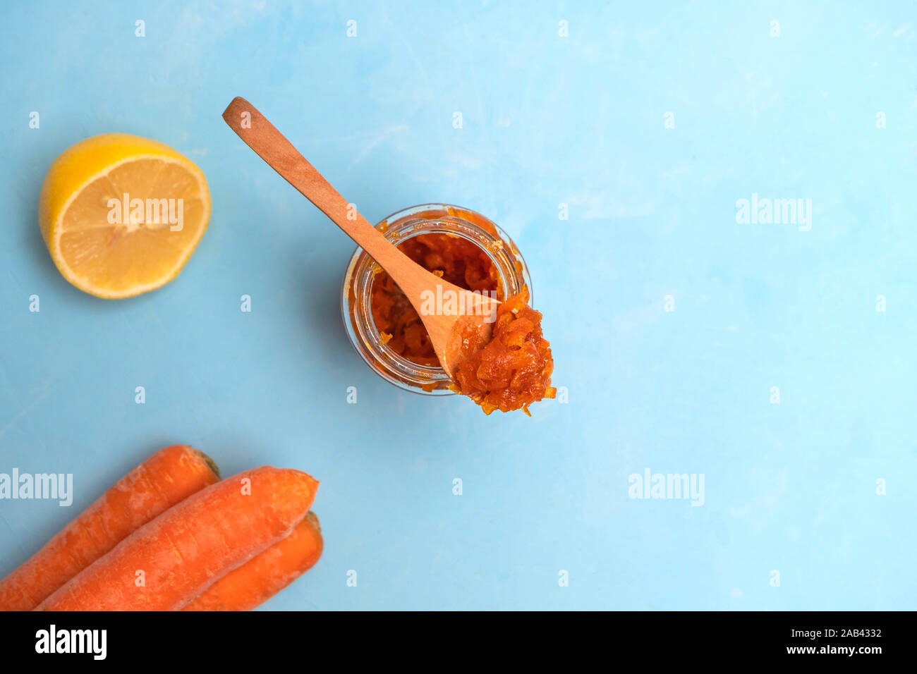 Homemade carrot jam in a glass jar with wooden spoon, fresh carrots and ...