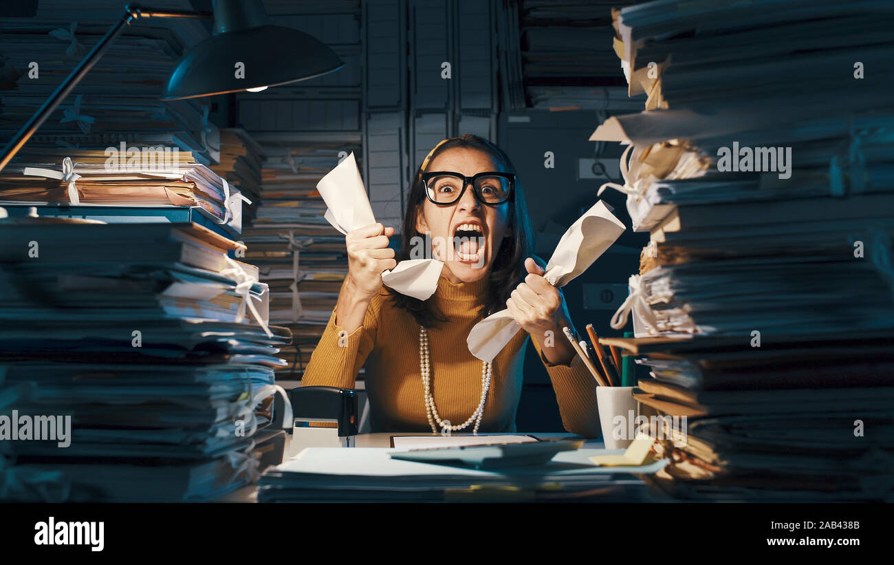 Angry stressed woman sitting at office desk screaming and crumpling ...