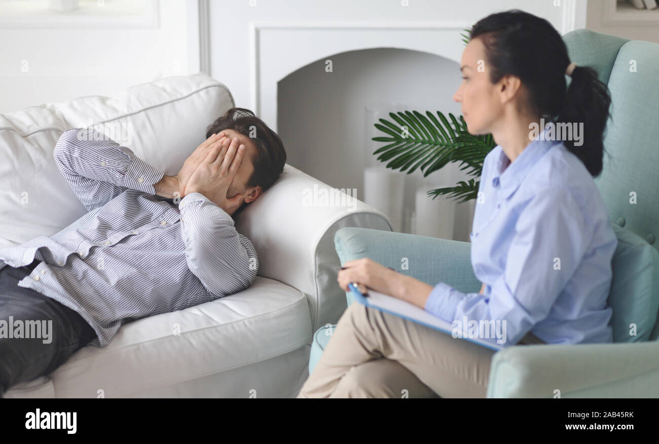 Crying deeply depressed man laying on coach at therapist office Stock ...