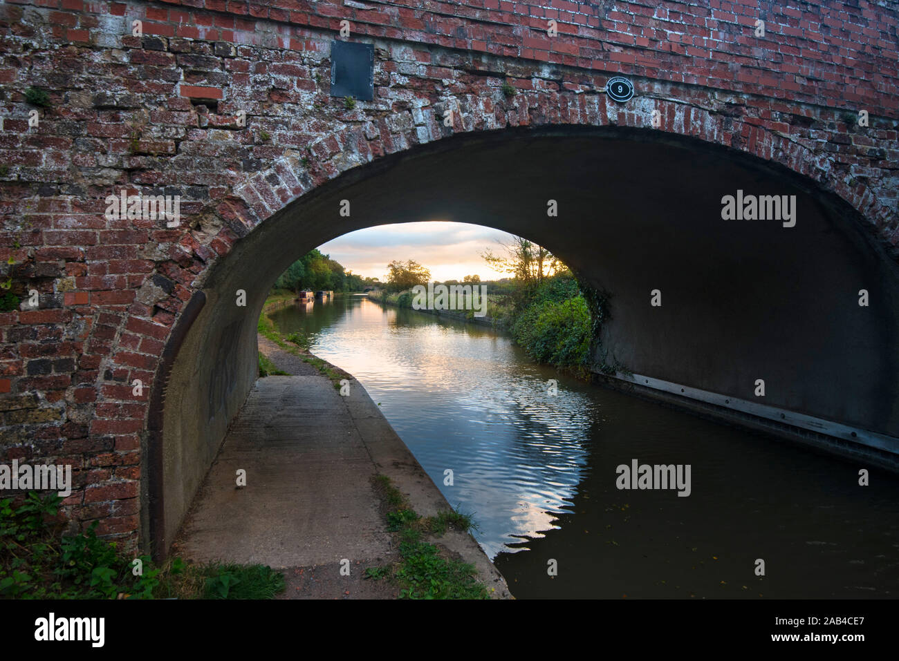 A foot path beside a canal leading under an old brick bridge to reveal ...