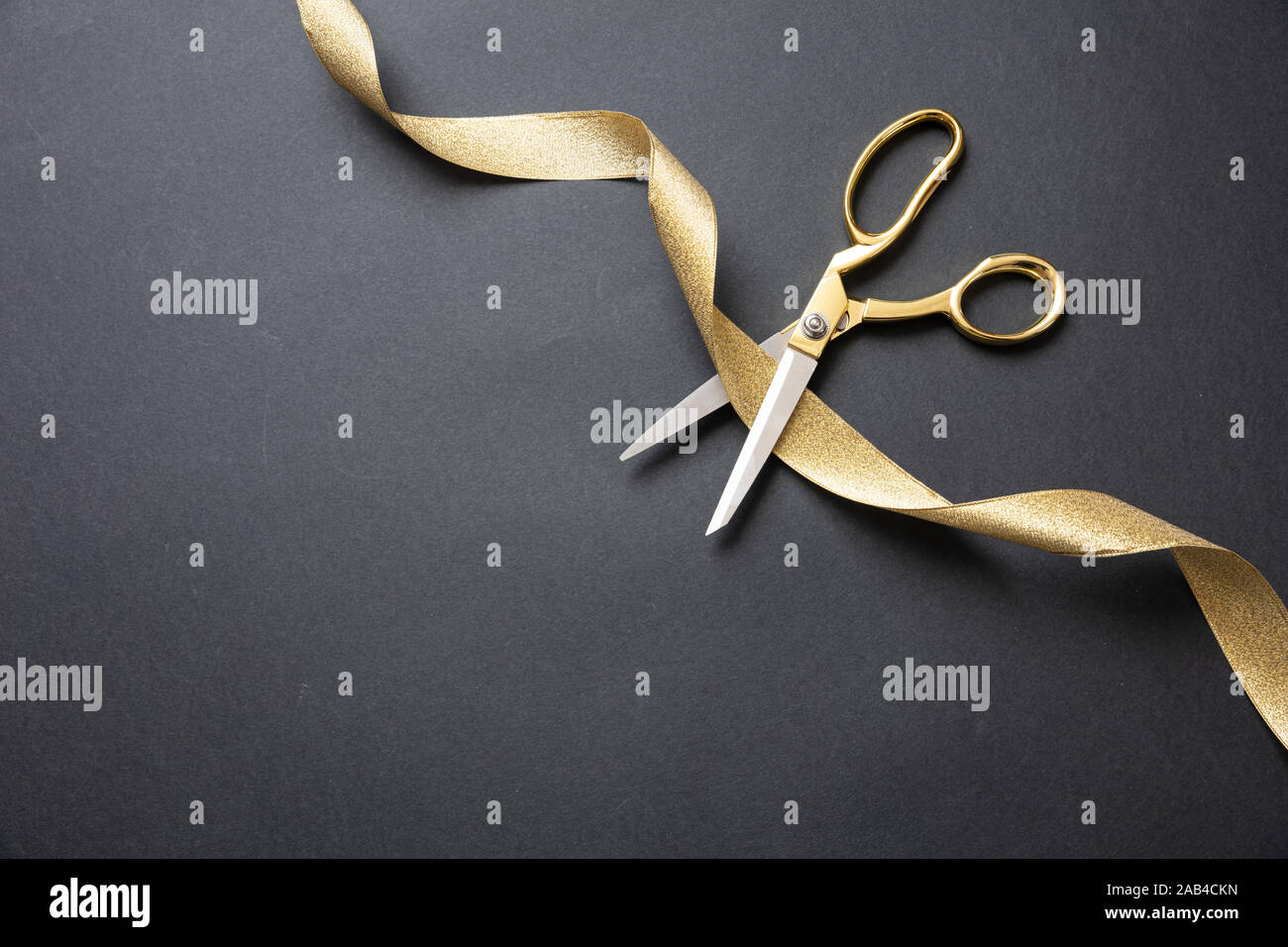 Grand opening. Gold scissors cutting gold silk ribbon, black background ...
