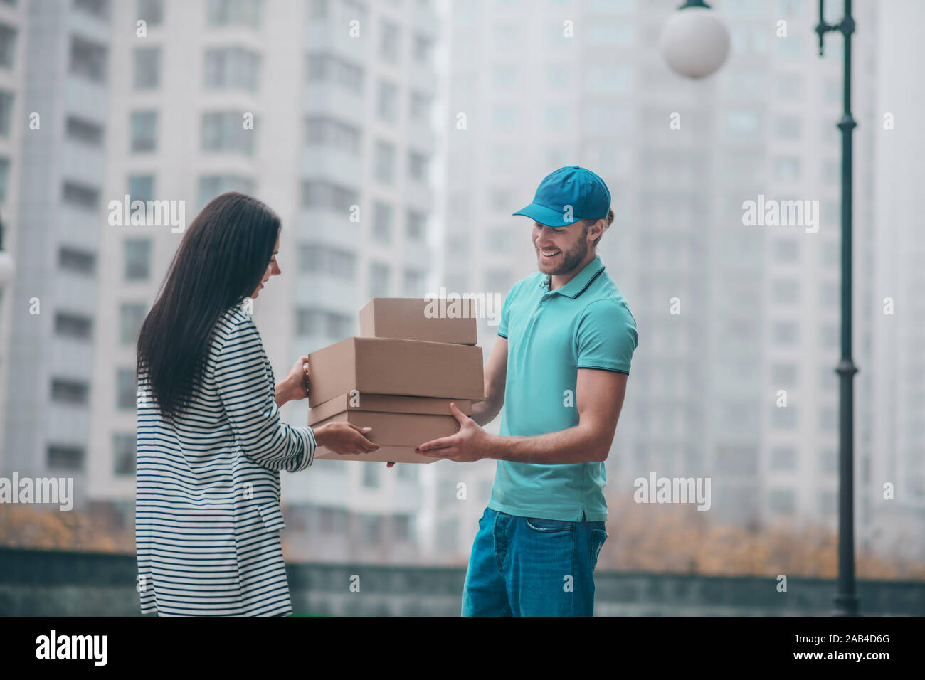 Woman taking boxes while meeting delivery man near building Stock Photo ...