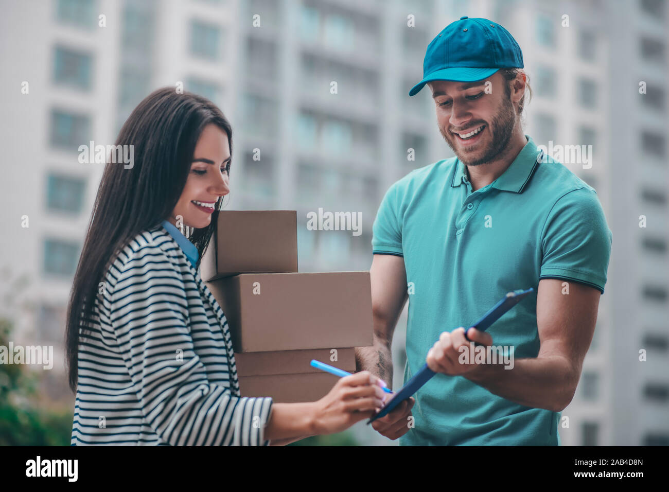 Delivery man smiling while giving declaration to pleasant client Stock ...