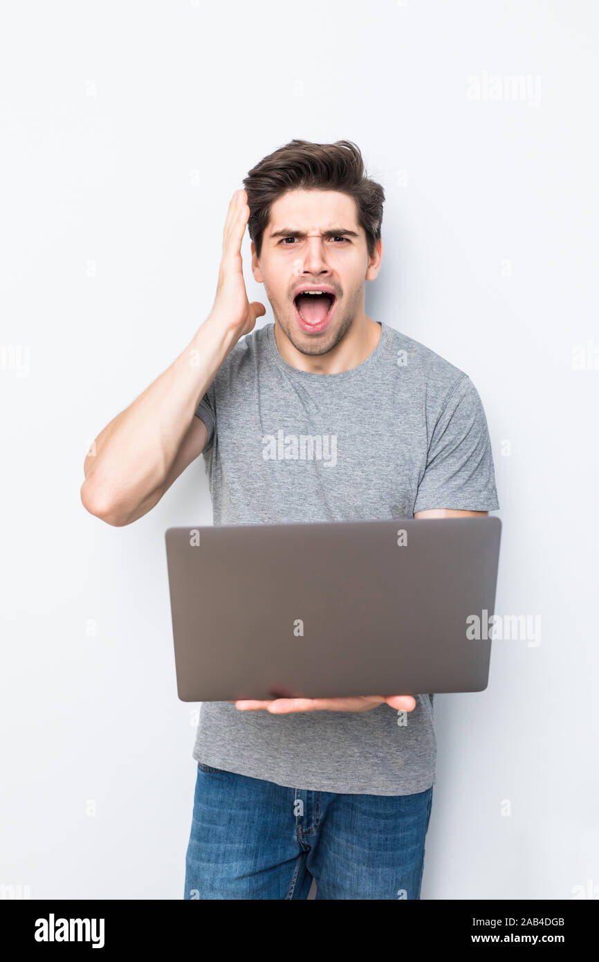 Angry upset man holding laptop and screaming over white background ...