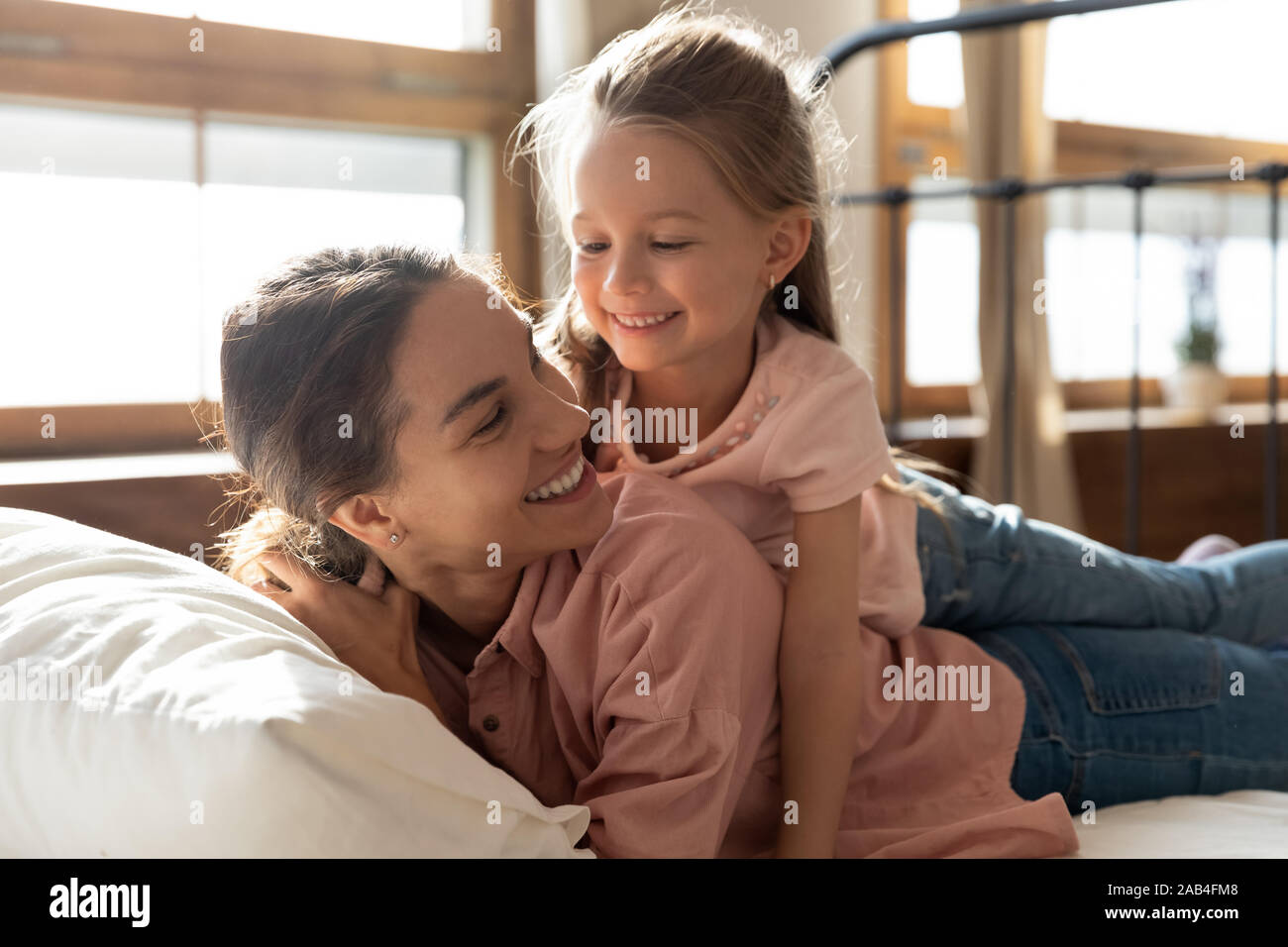 Happy affectionate mother and kid daughter laughing bonding on bed ...