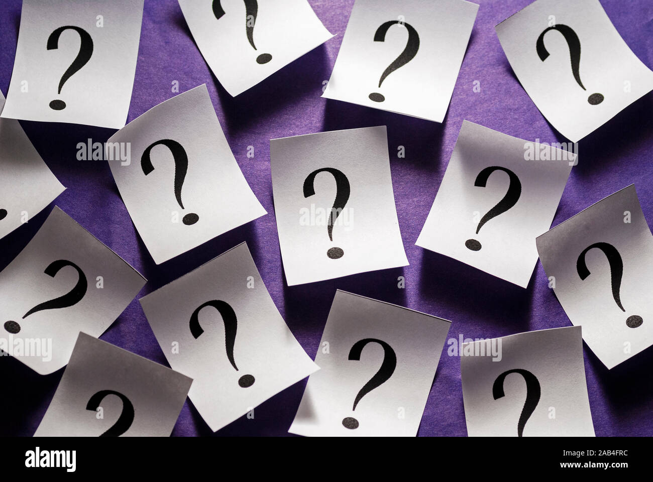 Randomly scattered question marks on white paper over a colorful purple ...