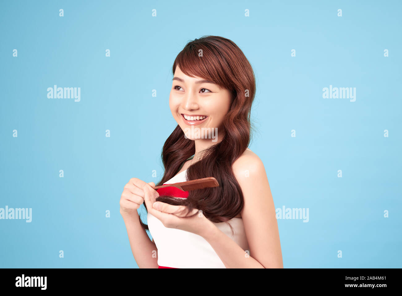 Beautiful young woman brush wonderful hair isolated on blue background ...