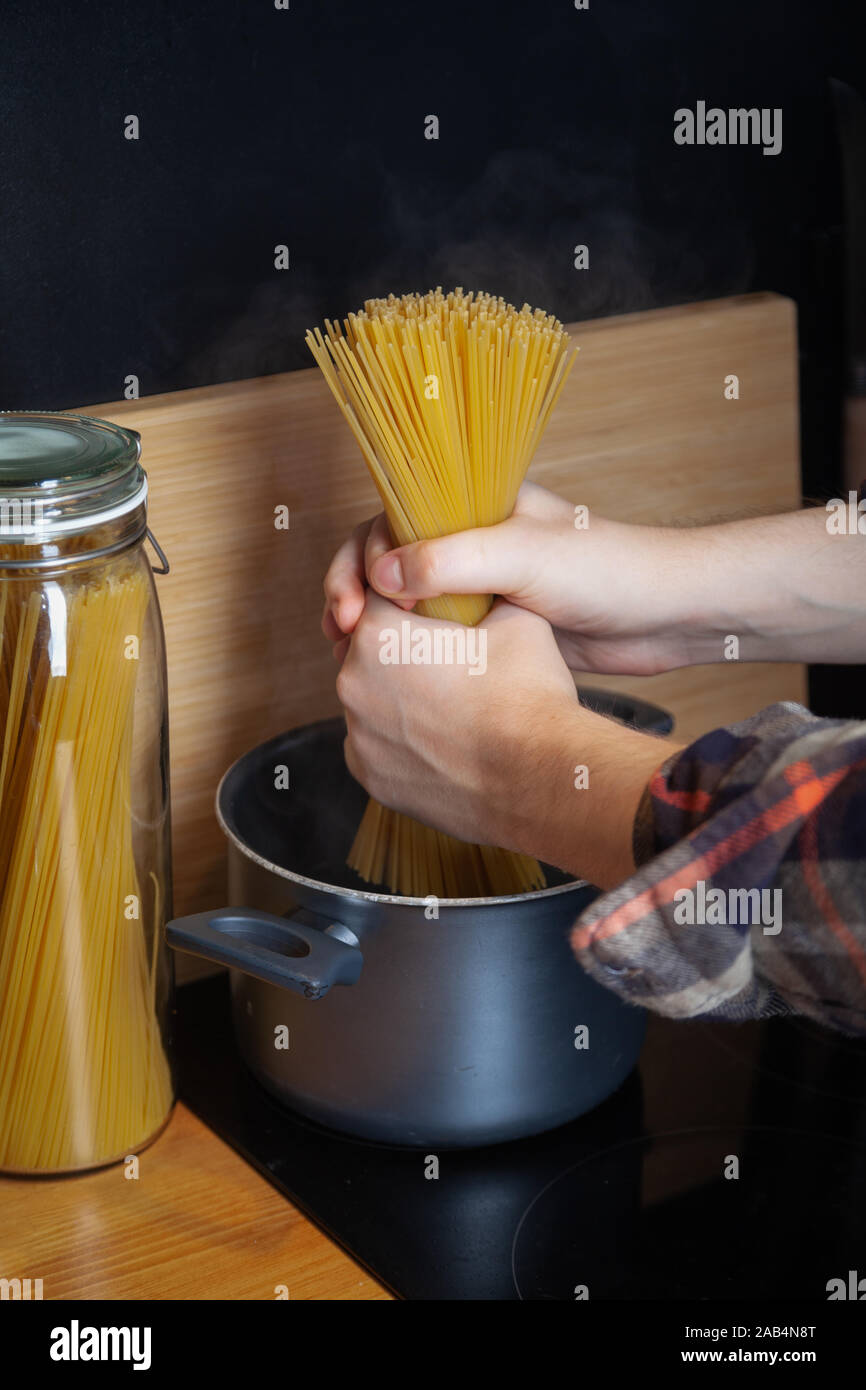 Cooking spaghetti in pot with boiling water, male hands put bunch of ...